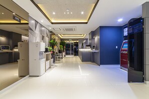 Um saguão de hotel moderno com uma mesa de recepção, um quiosque de autoatendimento e um chão limpo e reluzente.