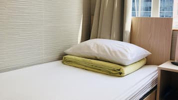 Cama arrumada com travesseiro branco e cobertor amarelo dobrado.