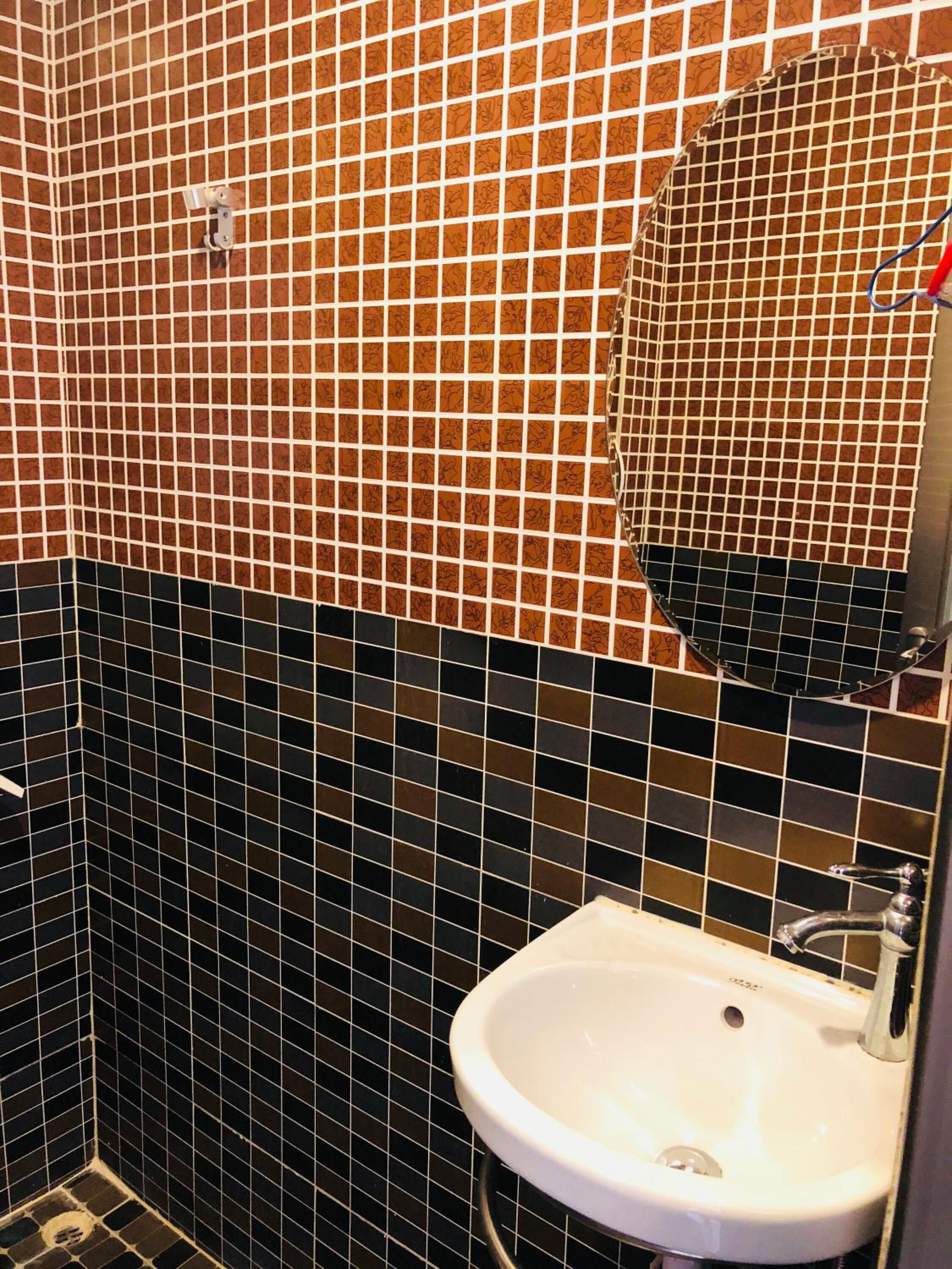 Um banheiro com pia branca, espelho e parede revestida com azulejos quadrados.