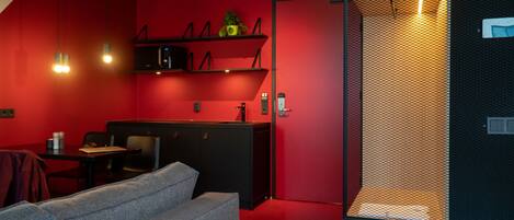 Quarto moderno com parede vermelha, sofá cinza, pequena mesa de jantar e guarda-roupa preto com porta de malha.