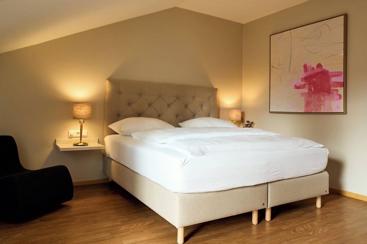Um quarto com uma cama grande, uma mesa de cabeceira, um abajur, uma cadeira e um quadro na parede.