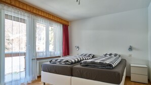 Quarto com duas camas, uma janela com cortinas, um radiador e uma mesa de cabeceira.
