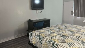Quarto de hotel com cama, escrivaninha, cadeira, televisão na parede e porta com cortinas.