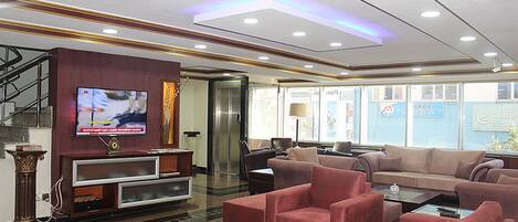 Um lobby moderno com televisão de tela plana, assentos confortáveis, balcão de recepção e uma escada.