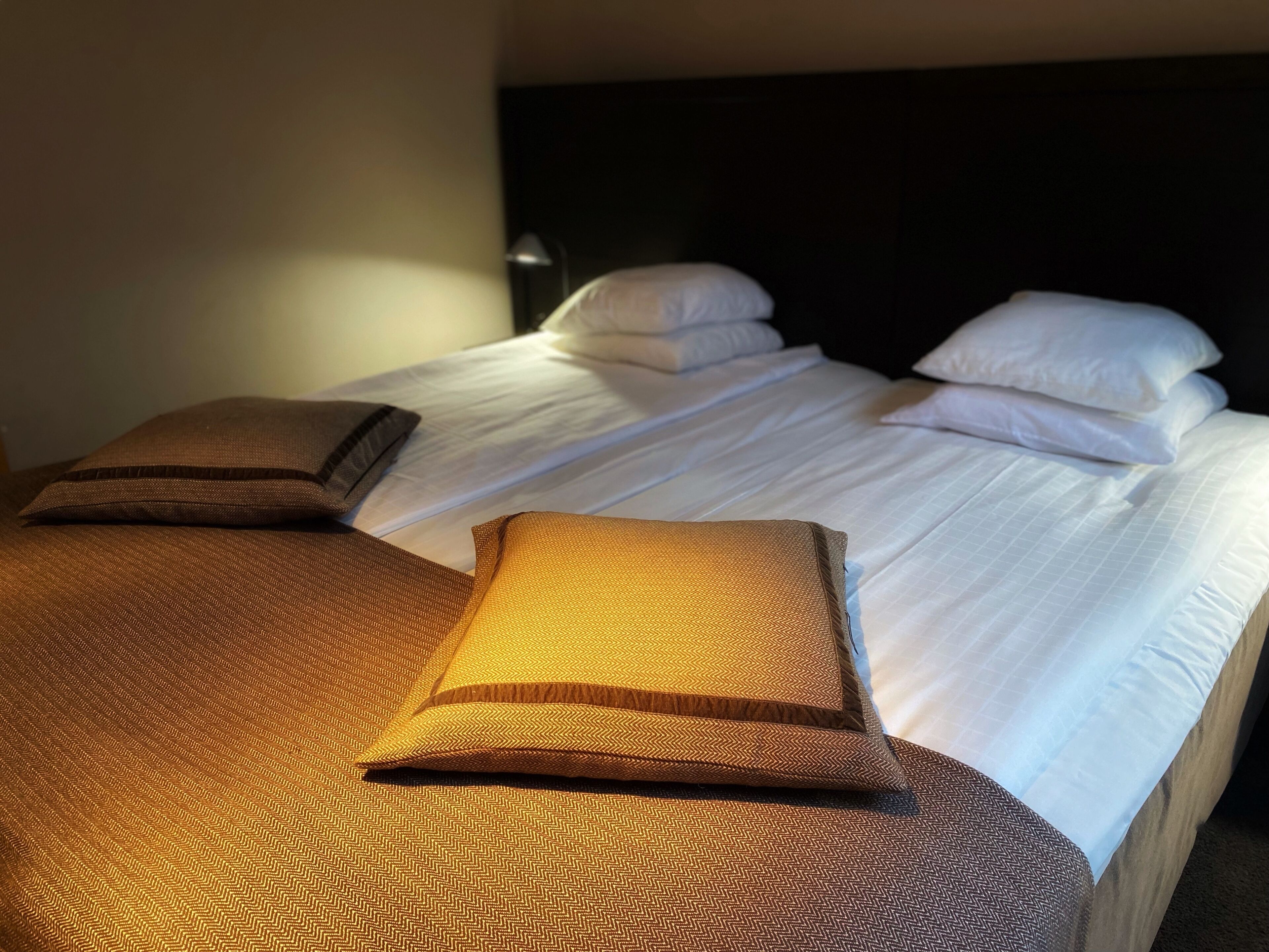 Cama bem arrumada com lençóis brancos e duas almofadas castanhas.