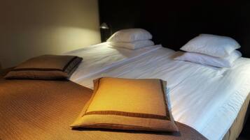Cama bem arrumada com lençóis brancos e duas almofadas castanhas.