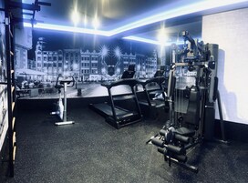 Uma academia com equipamentos de ginástica, esteira e espelho.