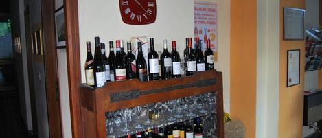 Uma adega com várias garrafas e copos de vinho, um relógio e um extintor de incêndio.