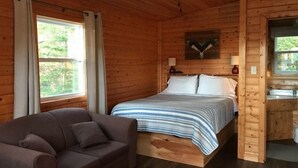 Quarto de cabana de madeira com uma cama, um sofá, um ventilador de teto e uma janela com cortinas.
