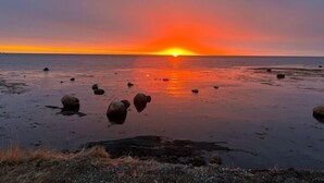 Uma praia com pôr do sol, rochas e águas calmas.