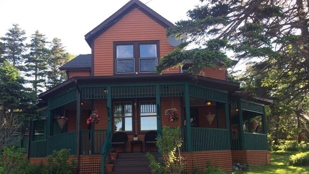 Uma casa de dois andares com varanda verde e um pequeno jardim frontal.