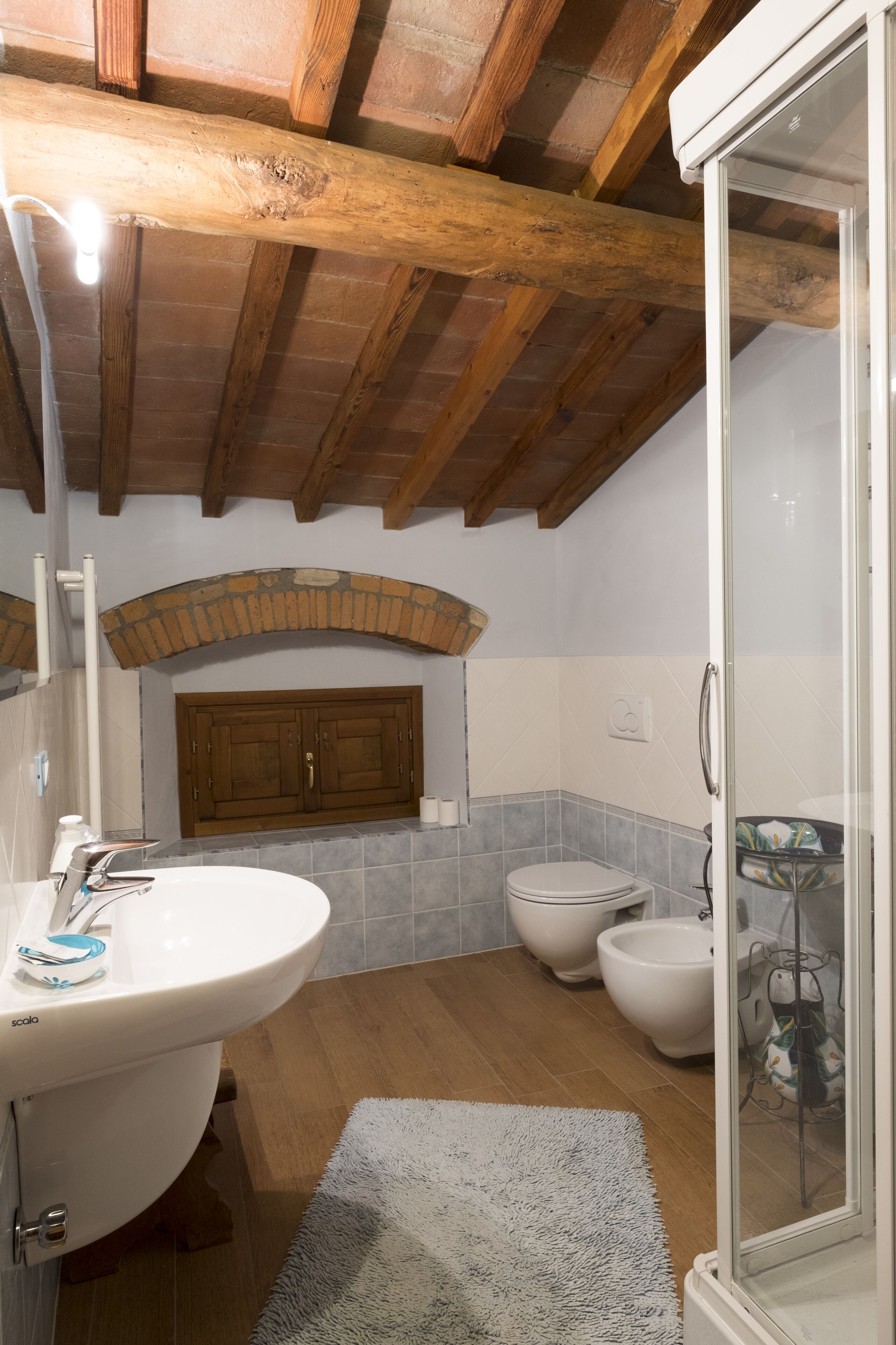 Casa de banho com teto de madeira, lavatório branco, bidé e cabine de duche em vidro.