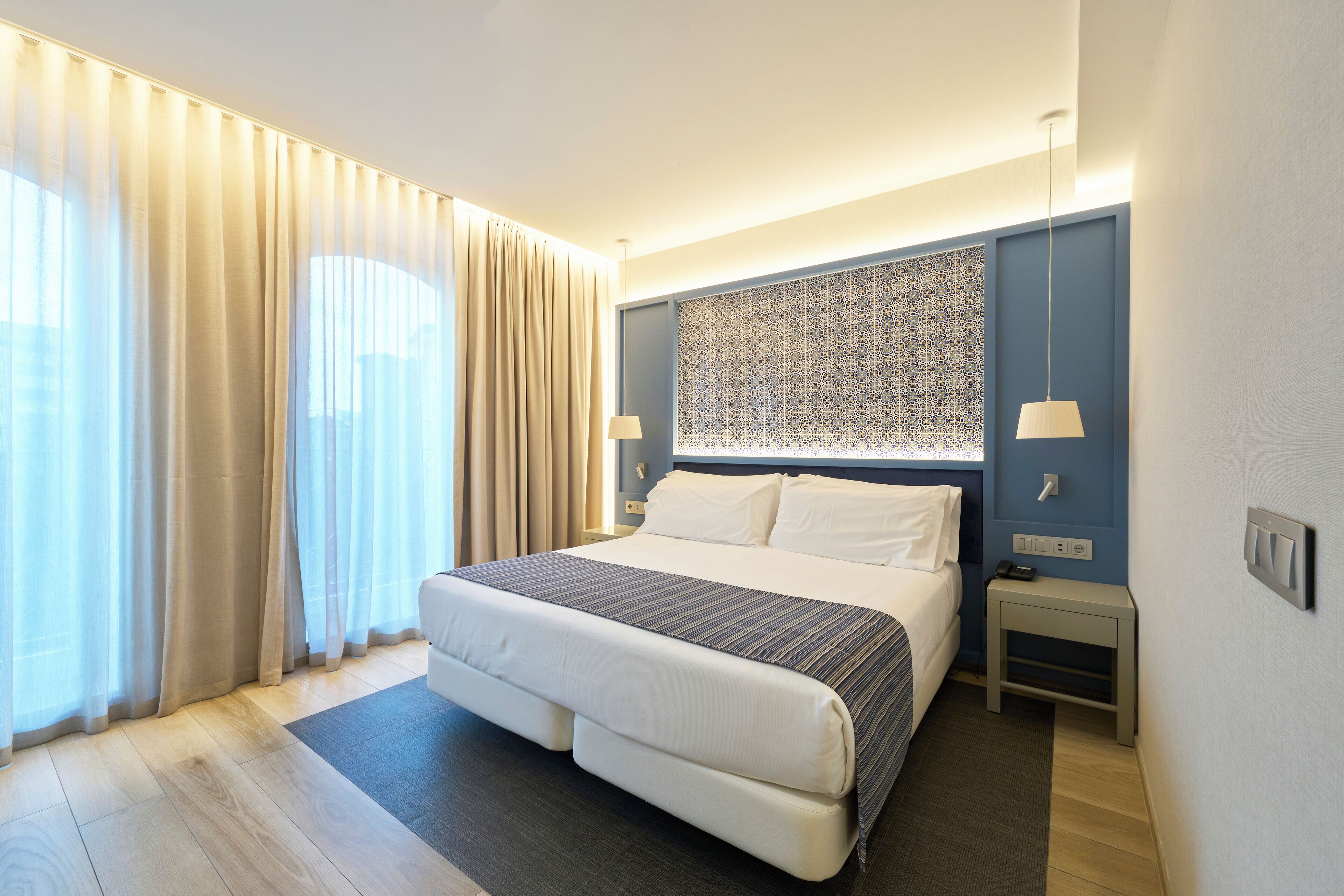 Quarto de hotel moderno com uma cama grande, uma mesa de cabeceira e uma luminária fixada na parede.