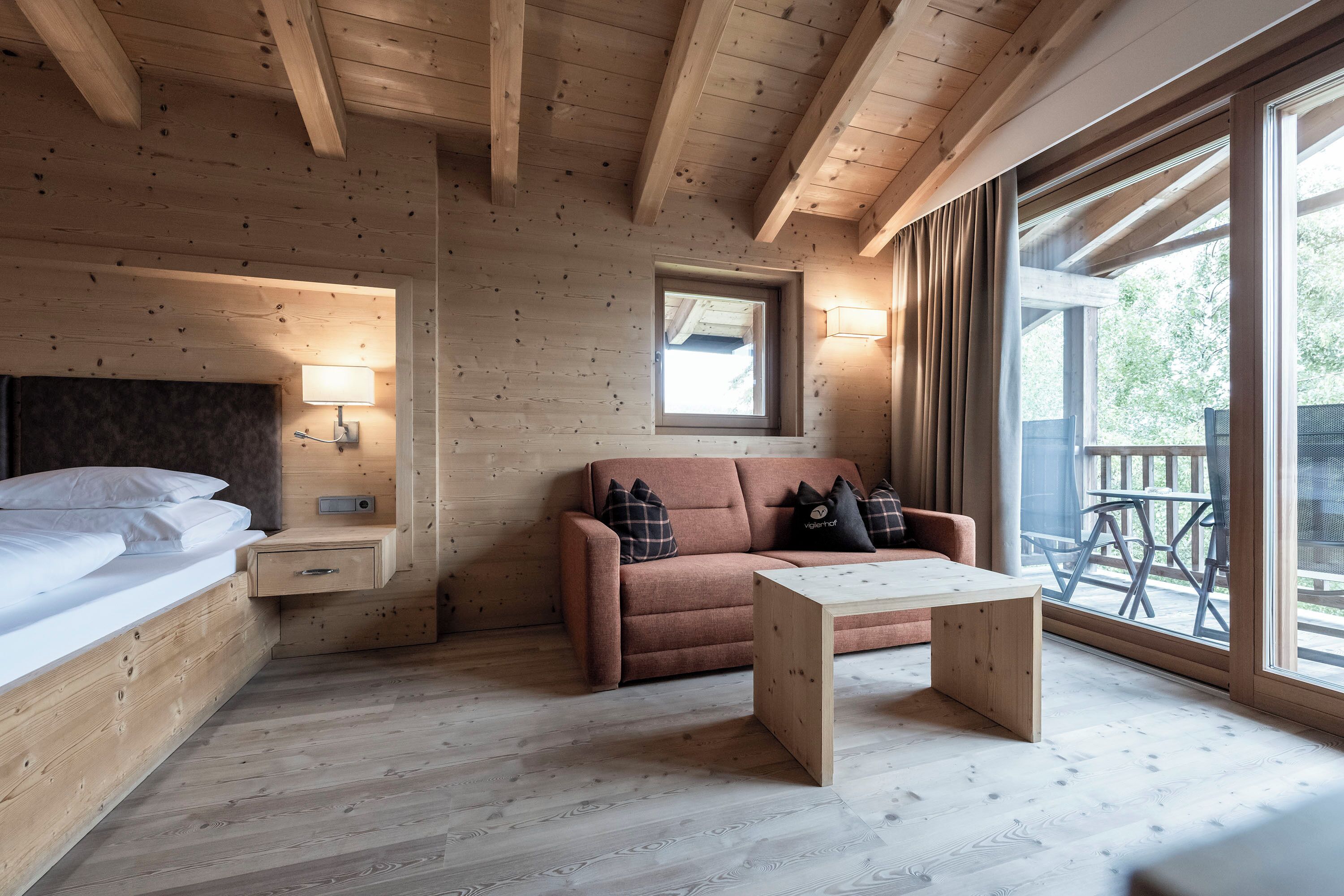 Quarto de cabana de madeira com cama, sofá, mesa e janela com vista para o exterior.