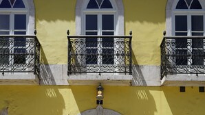 Um edifício amarelo com uma porta preta, duas plantas em vasos e uma placa com a inscrição 'Casa das Campainhas'.