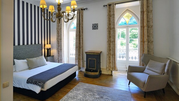 Quarto com cama, cadeira, lareira e janela com cortinas.