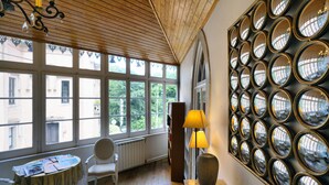 Quarto com janelas amplas, uma parede de espelhos, uma mesa com revistas, um abajur e um radiador.