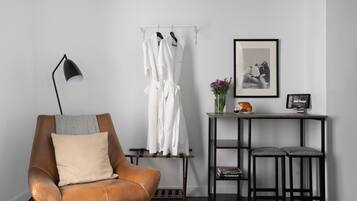Uma sala de estar moderna com uma poltrona de couro marrom, um roupão branco pendurado em um suporte, um quadro na parede, uma pequena mesa com um croissant e um abajur preto.
