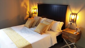 Cama bem arrumada com almofadas estampadas e mesa de cabeceira com abajur e um alto-falante.