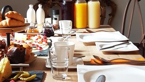 Uma mesa de jantar com diversos alimentos, incluindo doces, frutas e bebidas, com um espelho decorativo e um ventilador de teto ao fundo.