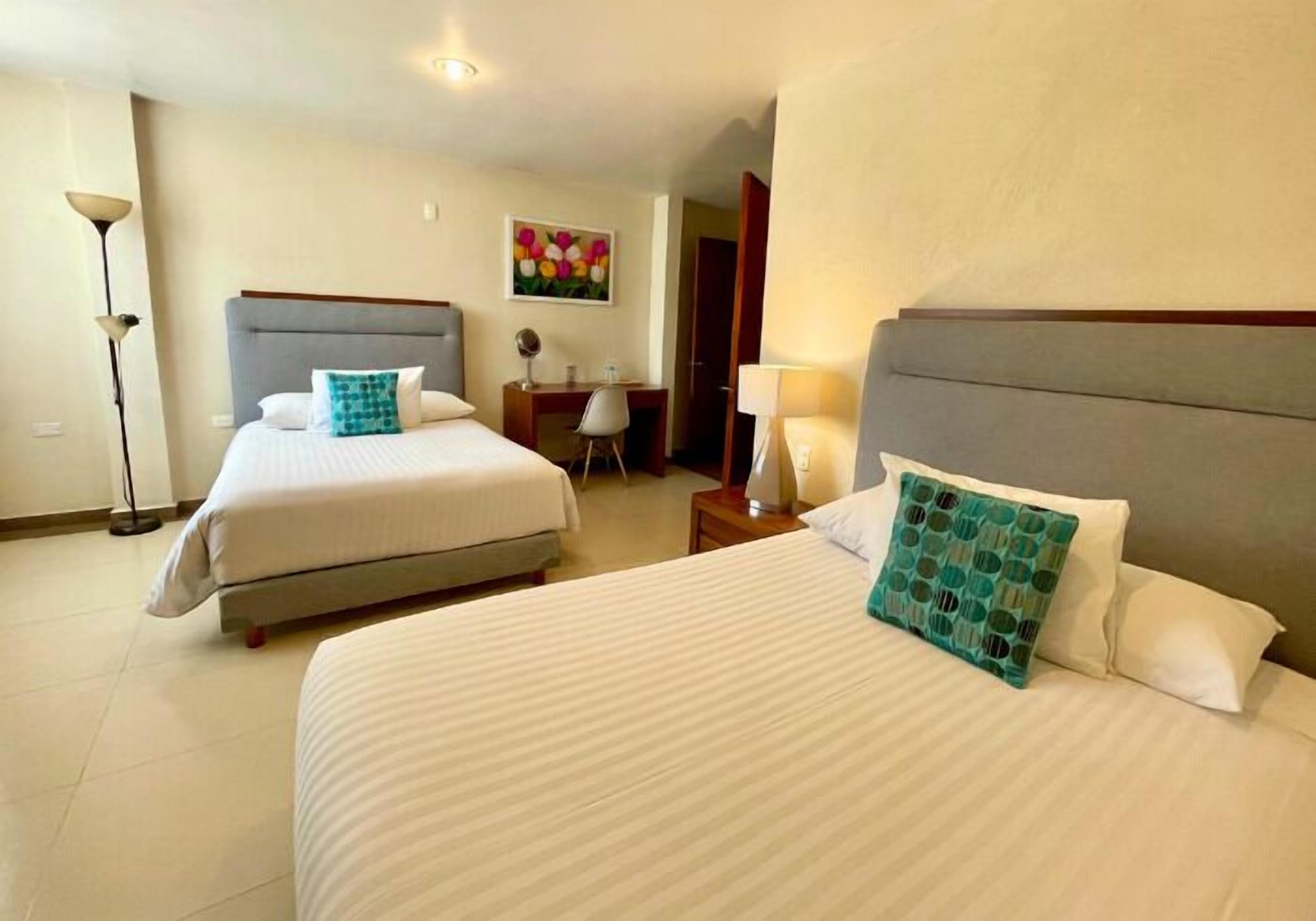 Quarto de hotel com duas camas, uma mesa e uma cadeira.