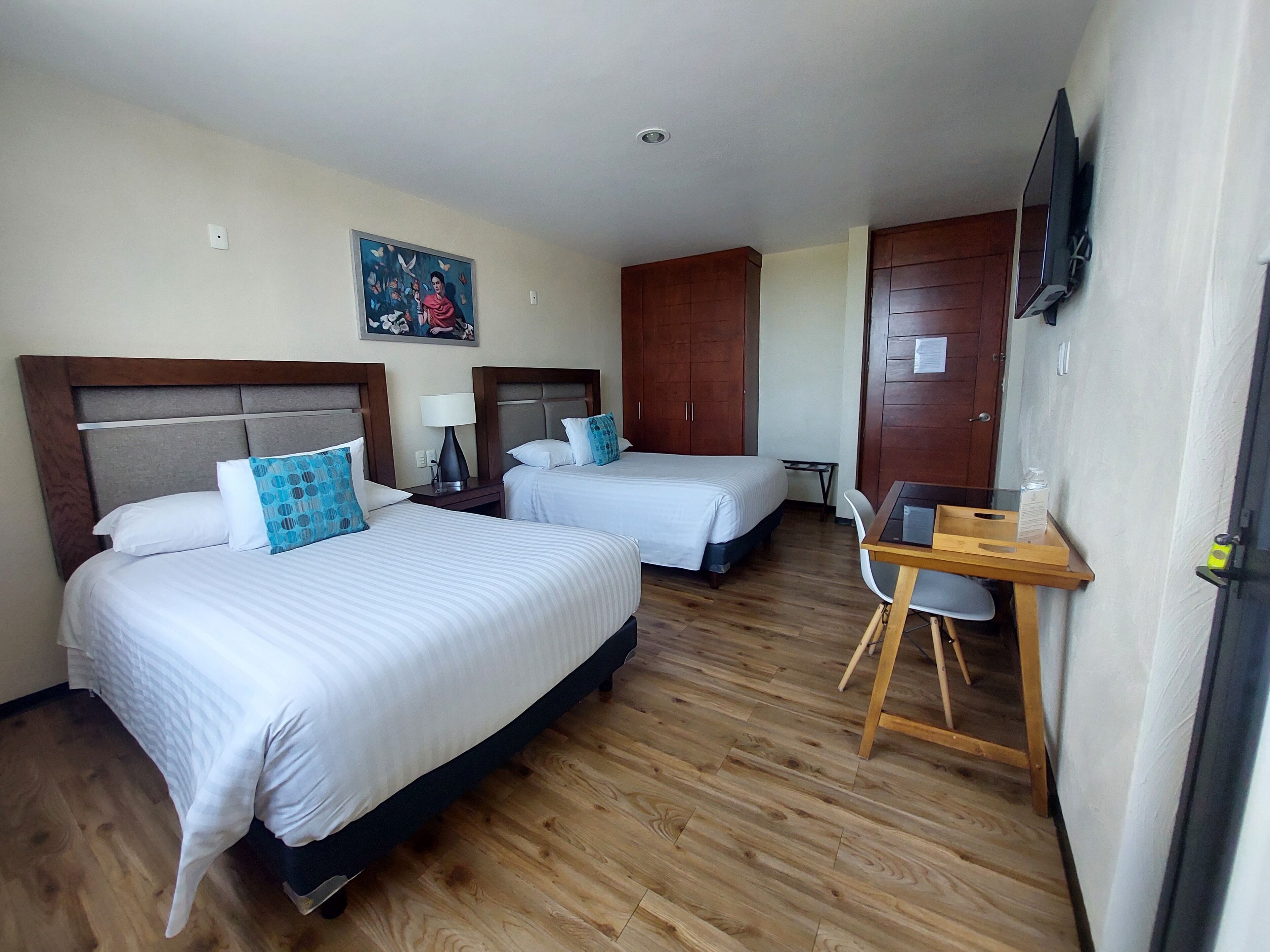 Quarto de hotel com duas camas, uma escrivaninha e uma televisão.