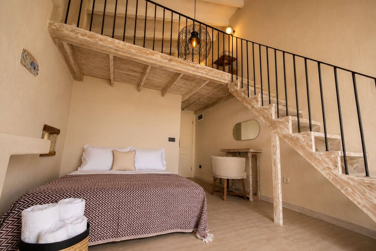 Um quarto com uma cama, uma cadeira, uma escrivaninha e uma escada de madeira.