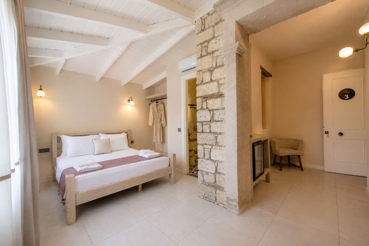 Quarto com cama, parede de pedra, porta e uma cadeira.