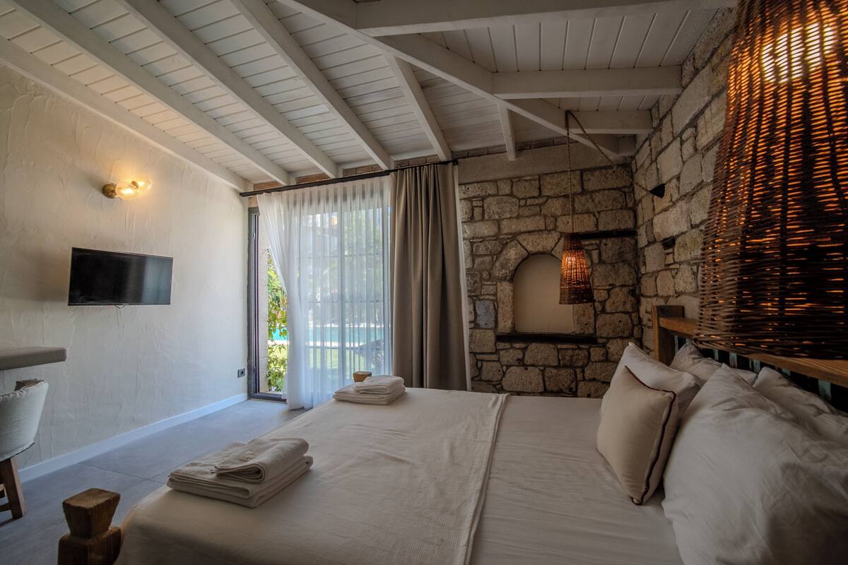 Quarto com parede de pedra, televisão de tela plana, cama com roupa branca e cabeceira de madeira.