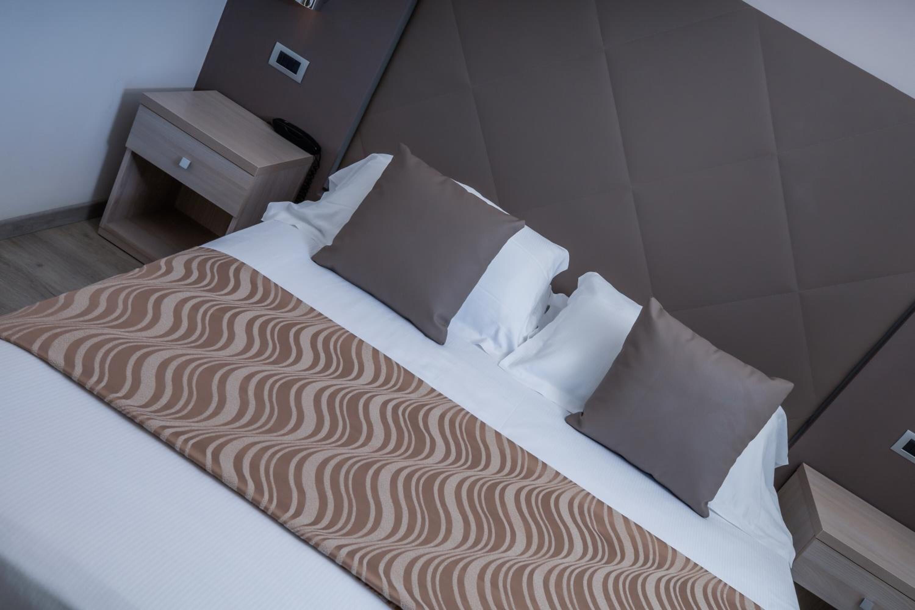 Cama bem arrumada com colcha estampada, duas almofadas e mesa de cabeceira com abajur.