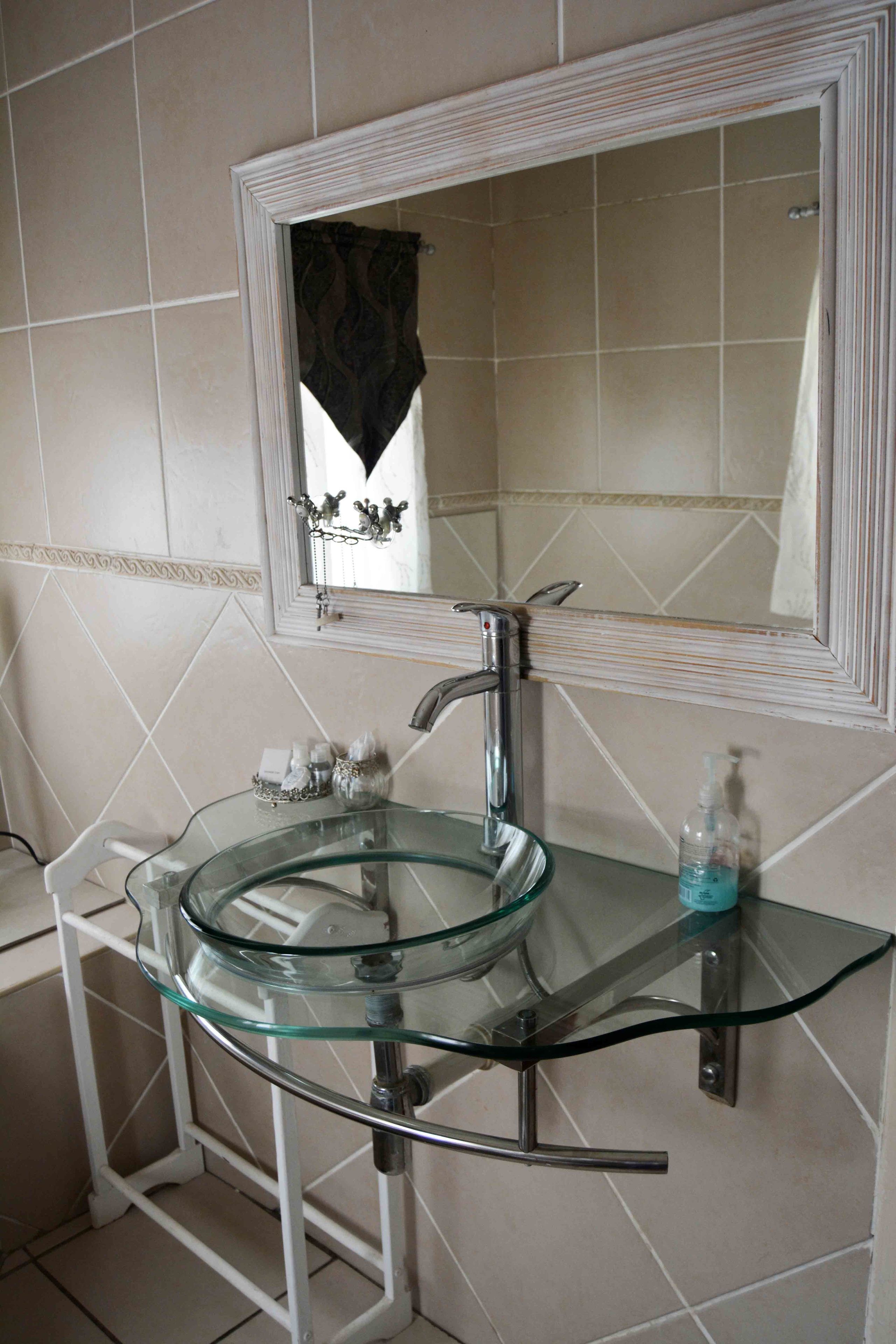 Uma casa de banho com lavatório de vidro, espelho e suporte para toalhas.