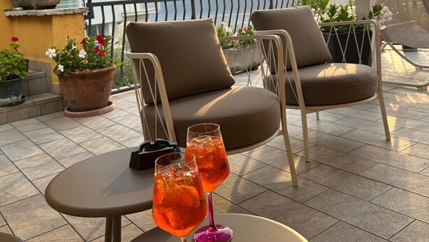 Um terraço com duas cadeiras, uma mesa e dois copos de bebida de laranja.
