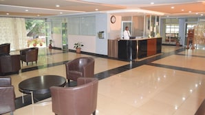 Um saguão de hotel com balcão de recepção, área de estar e plantas em vasos.