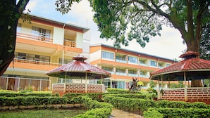 Um hotel com um pátio que apresenta um caminho, arbustos bem aparados e dois quiosques com telhado vermelho.