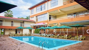 Piscina com espreguiçadeiras e guarda-sóis, prédio com várias varandas e placa indicando uma cafeteria.