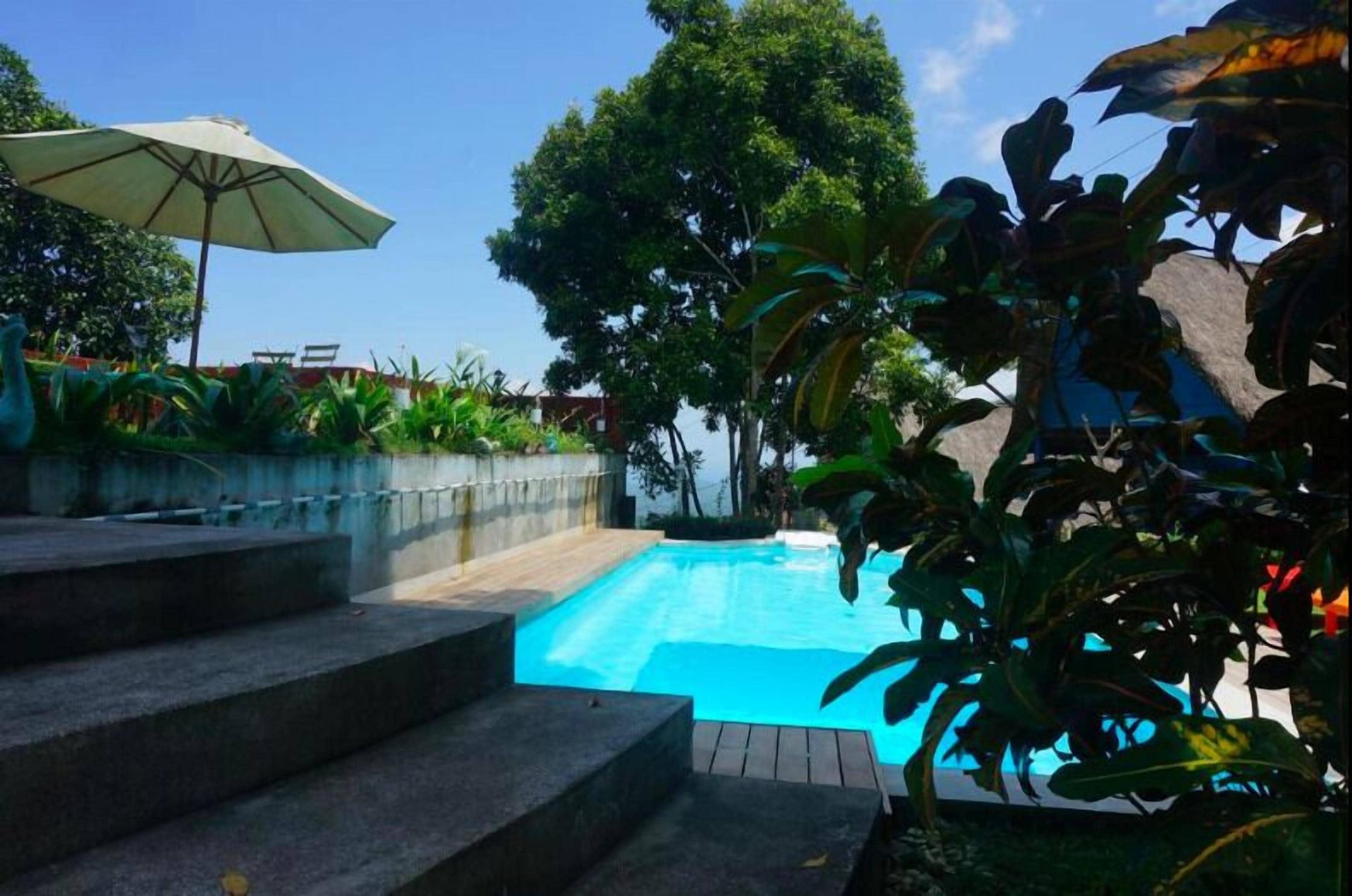 Piscina com escadas e volta a ser rodeada por vegetação exuberante e um céu azul límpido.