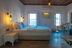 Quarto com cama, duas luminárias de cabeceira, uma cadeira, uma mesa e um quadro na parede.