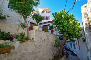 Uma rua estreita com edifícios brancos, uma árvore e uma placa indicando um hotel boutique.