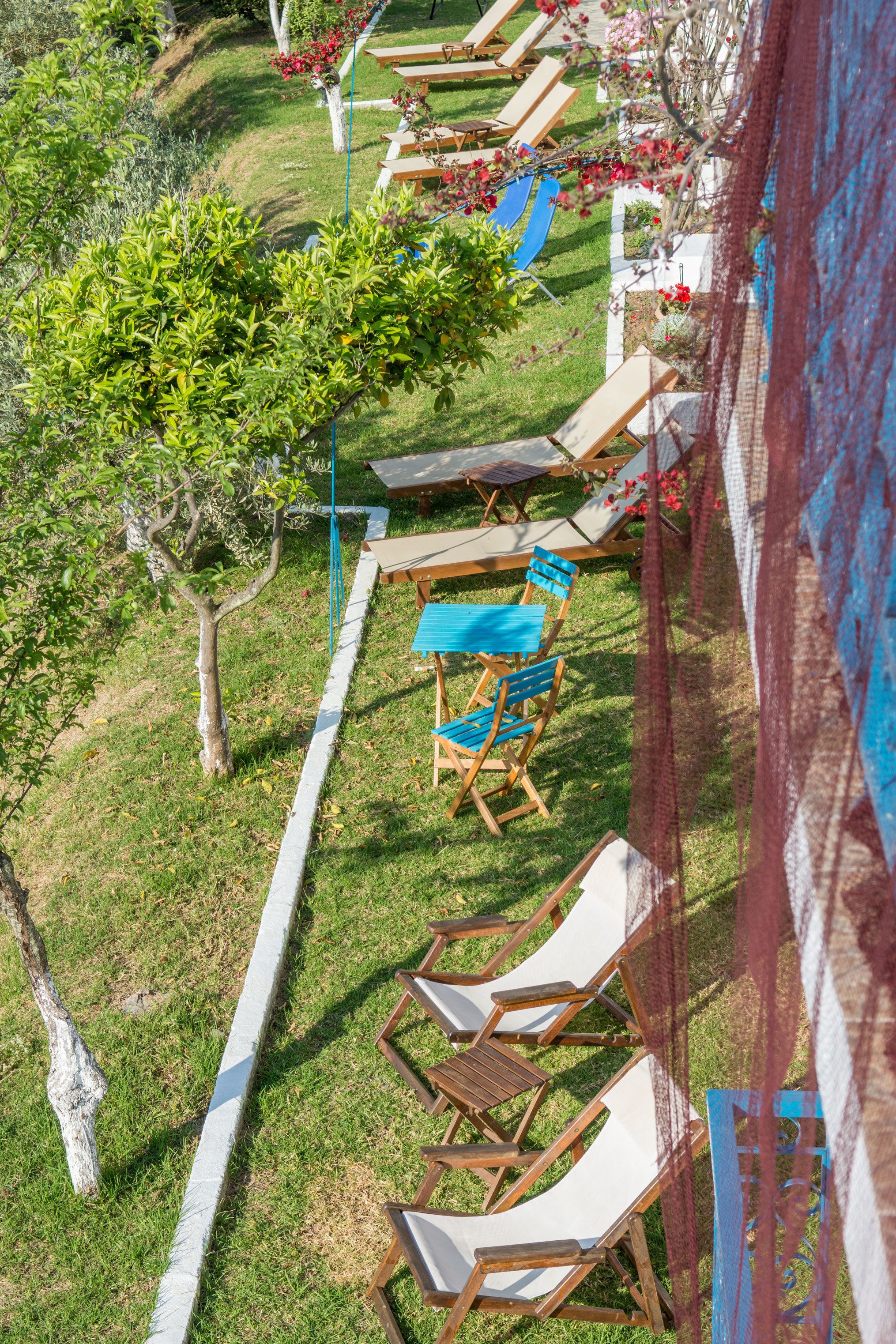 Área de jardim com cadeiras de descanso e uma pequena mesa, rodeada por vegetação e um tecido azul.