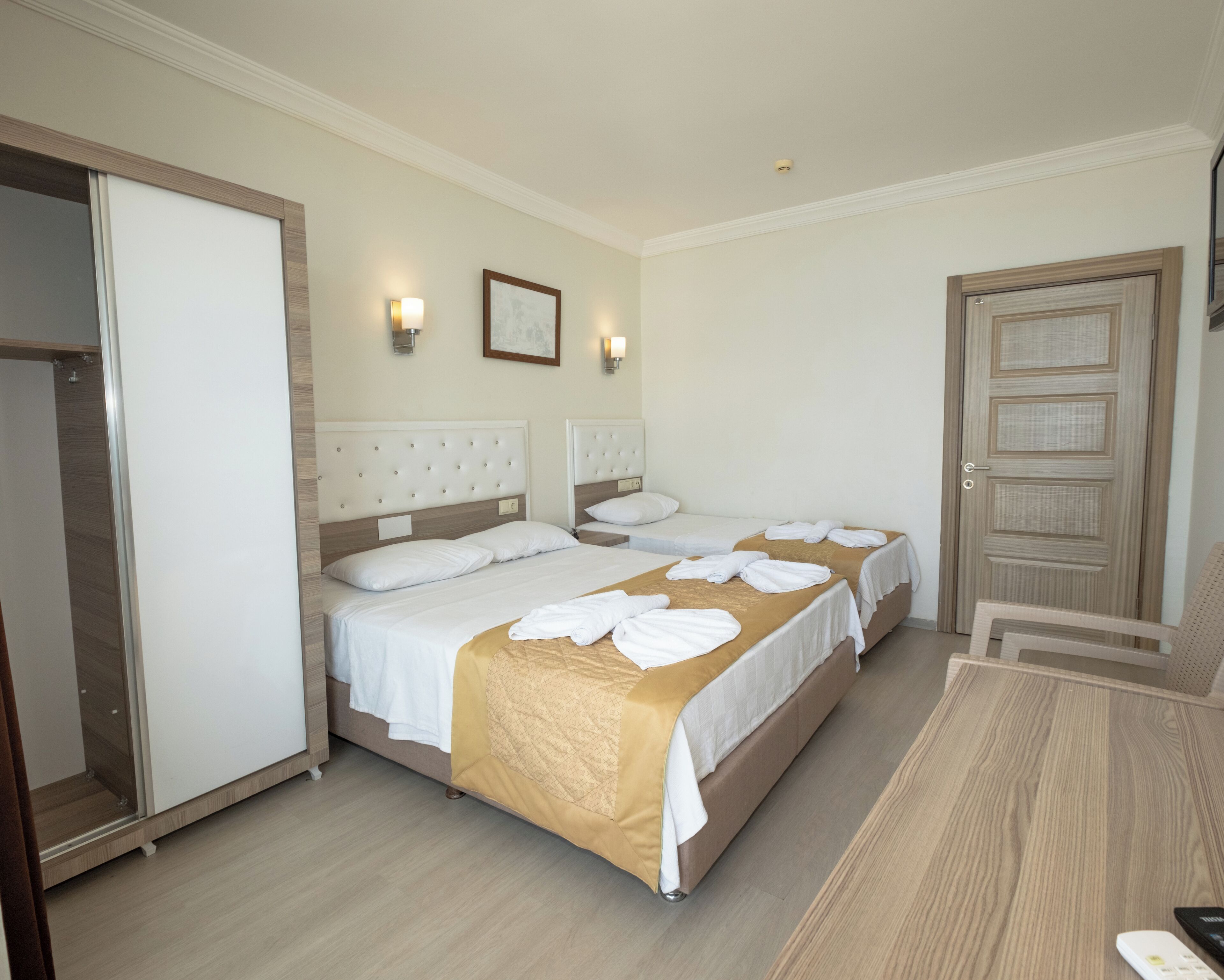 Quarto de hotel com duas camas, um guarda-roupa, uma escrivaninha e uma porta.