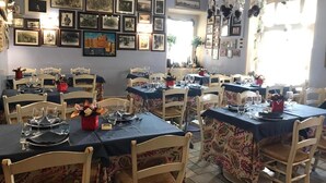 Uma sala de jantar com mesas postas, cadeiras e uma parede decorada com quadros.