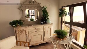 Quarto com um armário branco, um espelho, uma pequena mesa redonda com uma planta e uma cadeira de vime.