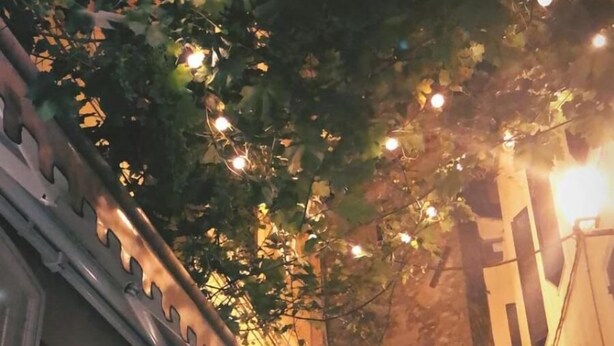Um beco estreito com paredes de pedra, uma escadaria e luminárias pendentes.