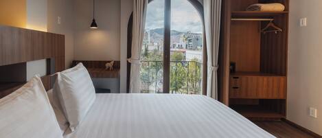 Quarto de hotel com uma cama grande, um guarda-roupa de madeira, uma varanda com vista para edifícios e um lustre.