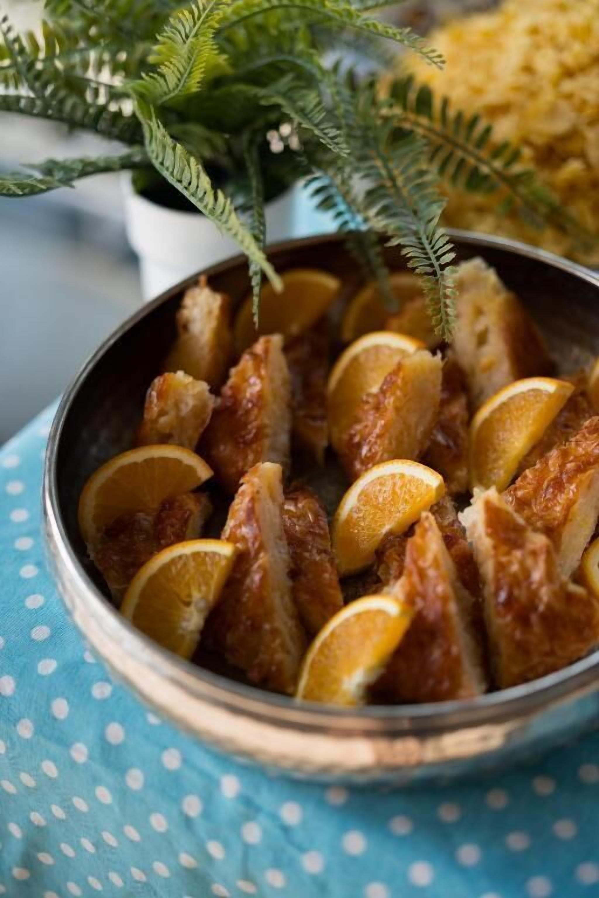 Uma tigela de pão com fatias de laranja sobre um tecido azul com bolinhas.