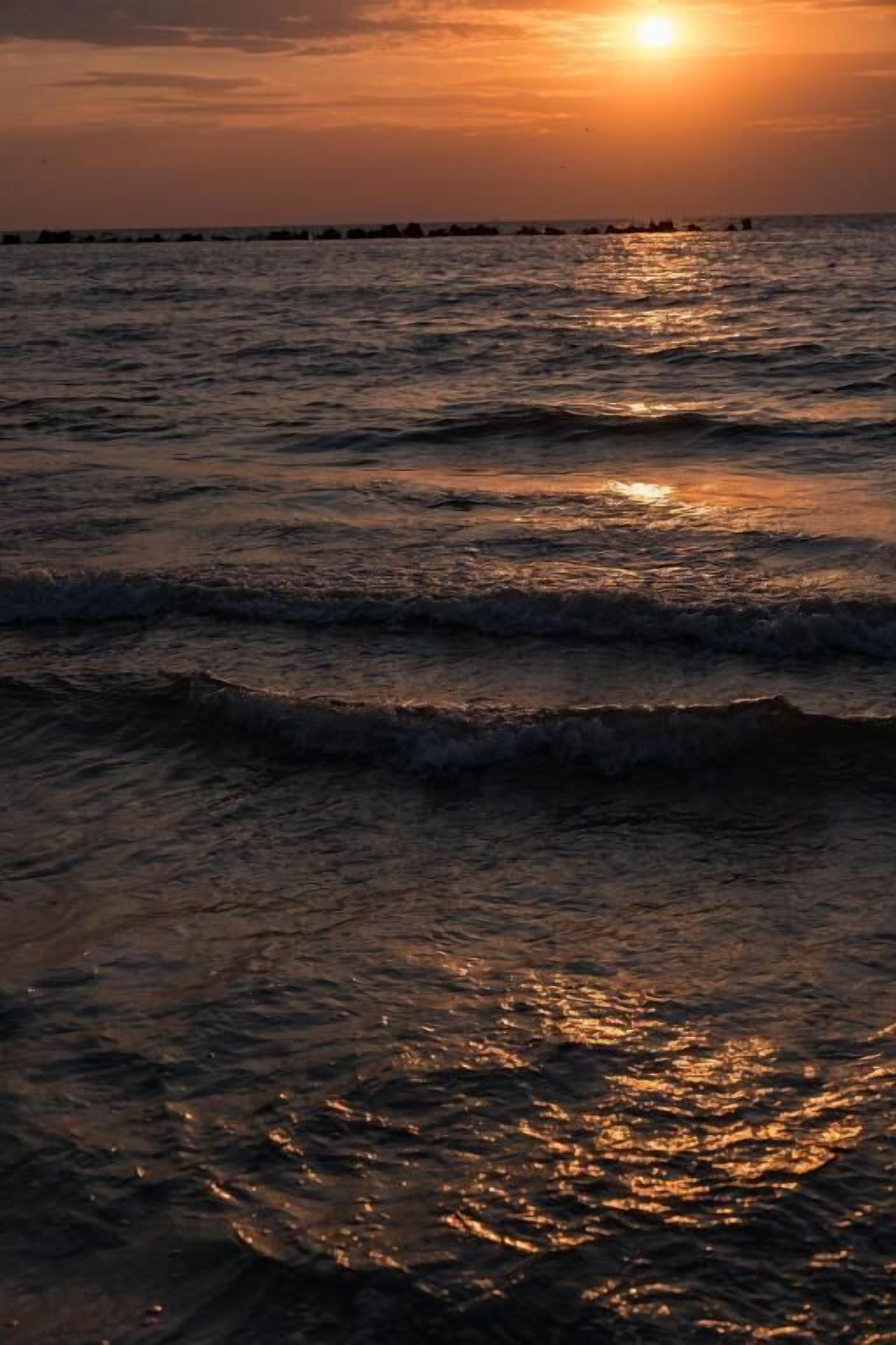 Um pôr do sol sobre o oceano, com ondas refletindo a luz do sol.
