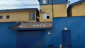 Um edifício com fachada azul e amarela, telhado com telhas e entrada com portão.