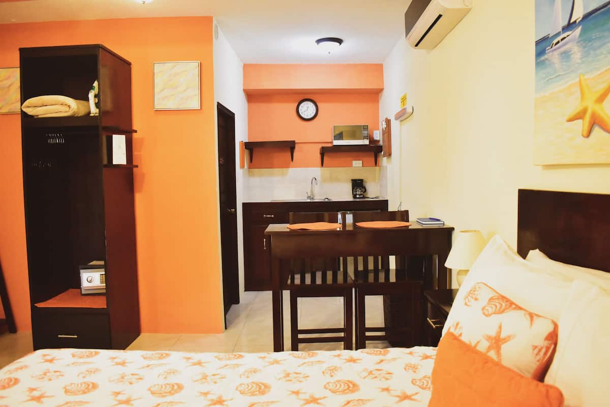 Quarto de hotel compacto com cama, pequeno espaço de cozinha e área de refeições.
