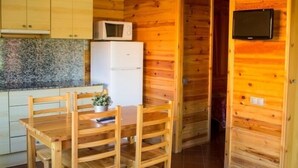 Interior de uma cabana de madeira, com cozinha equipada, incluindo micro-ondas, frigorífico e mesa de jantar com cadeiras.