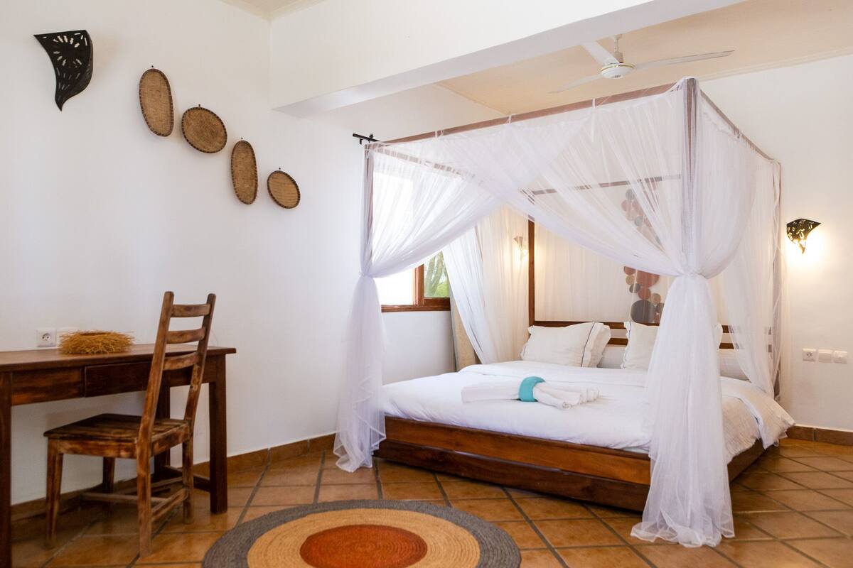 Quarto com cama de dossel, escrivaninha de madeira e uma cadeira.